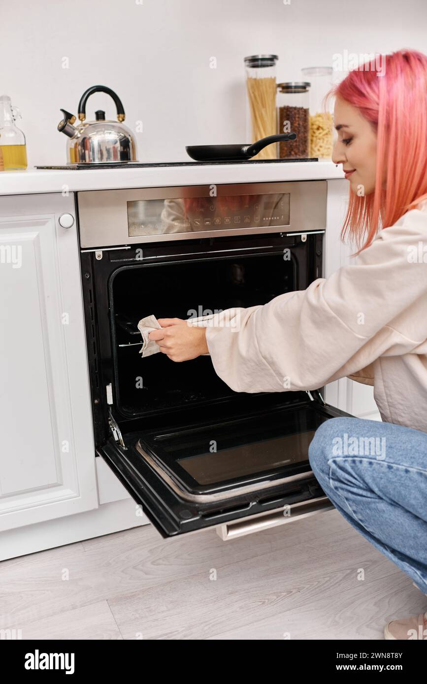 young appealing woman with pink hair in casual cozy attire using oven ...