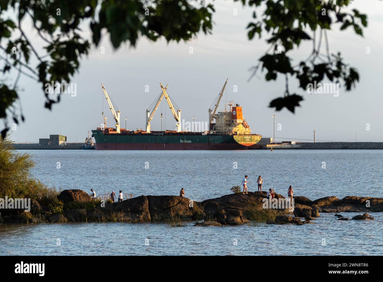 People walking on a set of rocks, while a cargo ship in the background ...