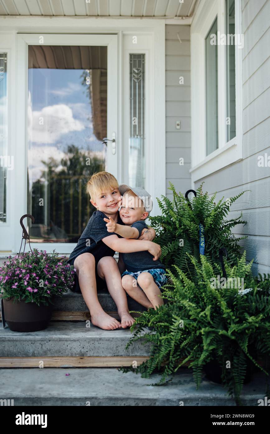 Two brothers hugging on front steps in summer near flowers Stock Photo ...