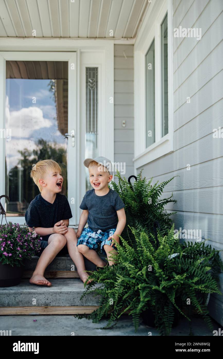 Two young boys laugh at each other on front step in summer Stock Photo ...