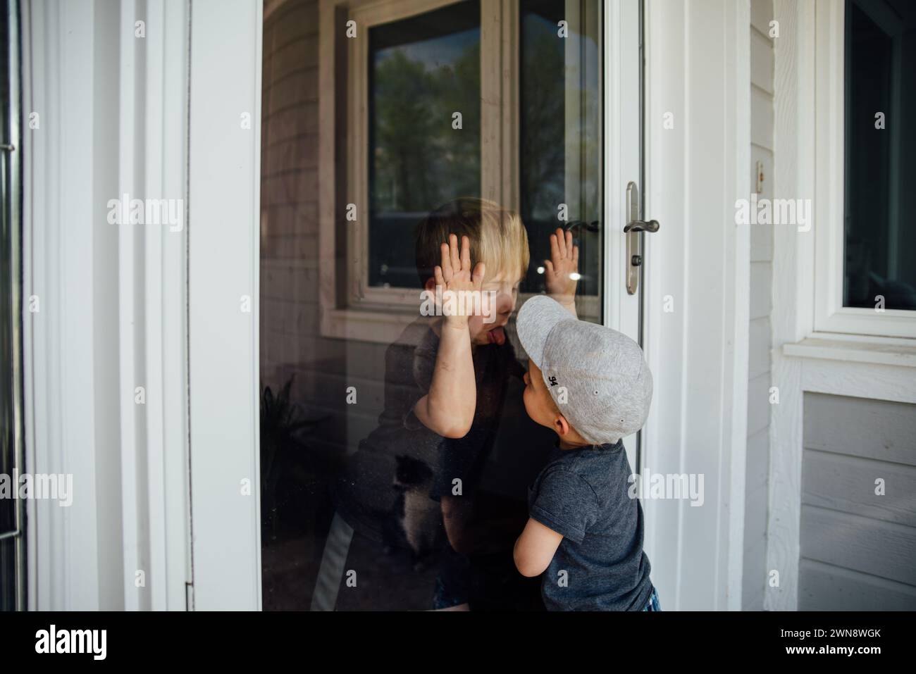 Two boys make faces at each other through a glass window Stock Photo ...