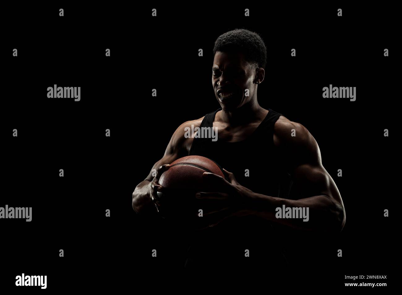 Basketball player holding a ball against black background. Screaming ...