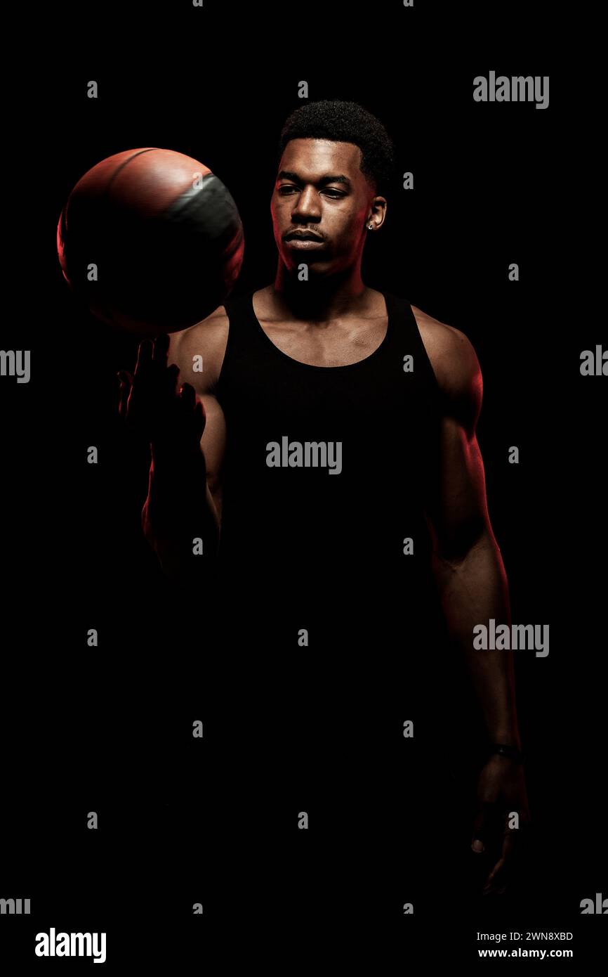 Basketball player side lit with red color holding a ball against black ...
