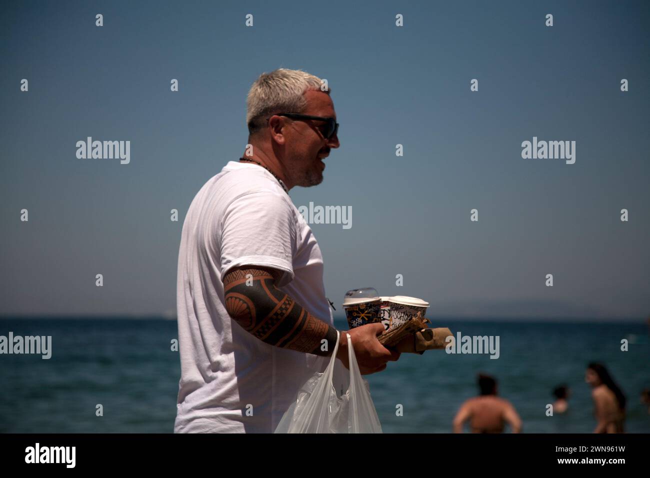 holidaymaker carrying drinks on beach vouliagmeni athens riviera greece ...