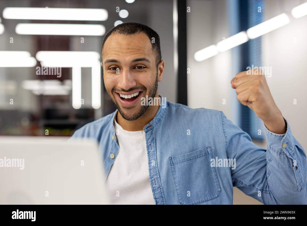 An exuberant young man in a light blue denim shirt punches the air with ...