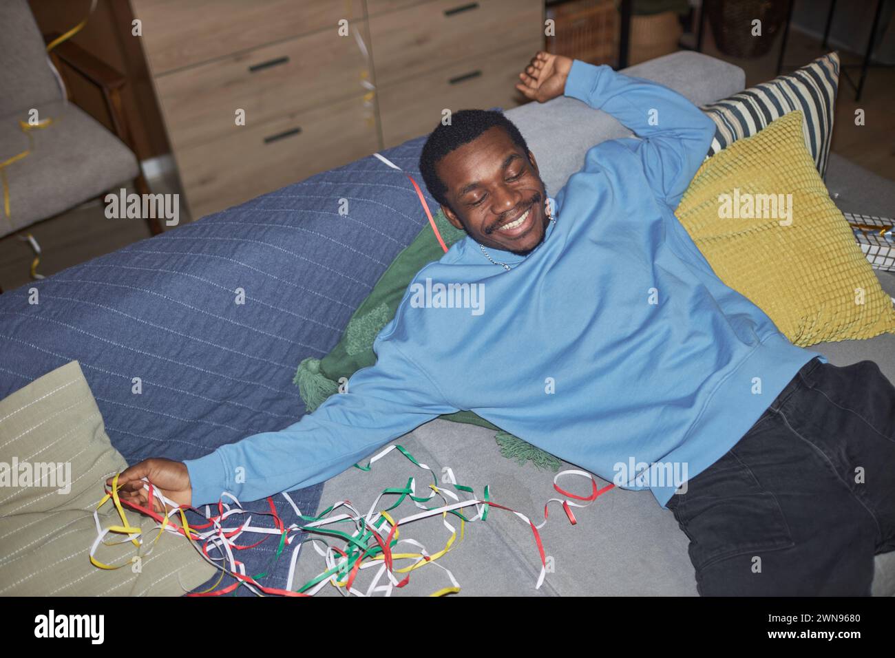 High angle portrait of smiling Black man falling on couch with confetti ...