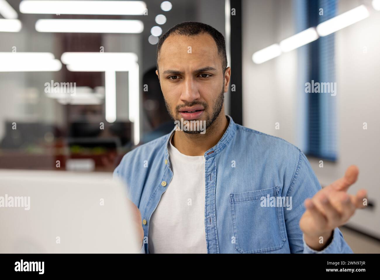 A young male professional in a blue denim shirt appears perplexed and ...