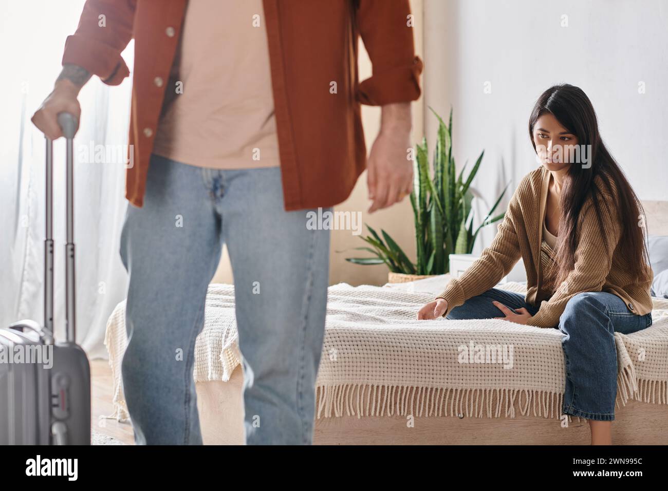 depressed asian woman sitting on bed while her husband with suitcase ...