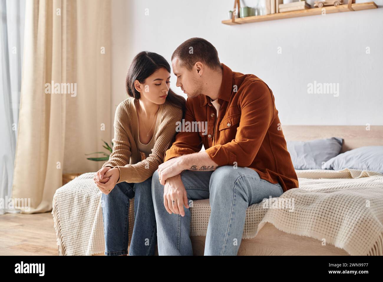 Young And Sad Interracial Couple Sitting And Talking On Bed At Home