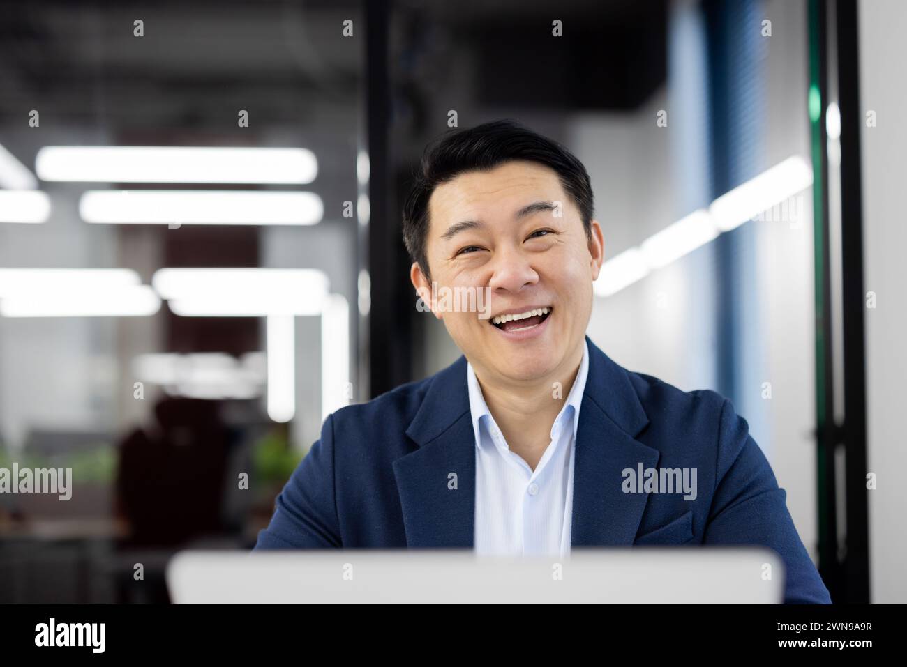 Portrait of happy japanese man in blue suit looking at camera with wide ...