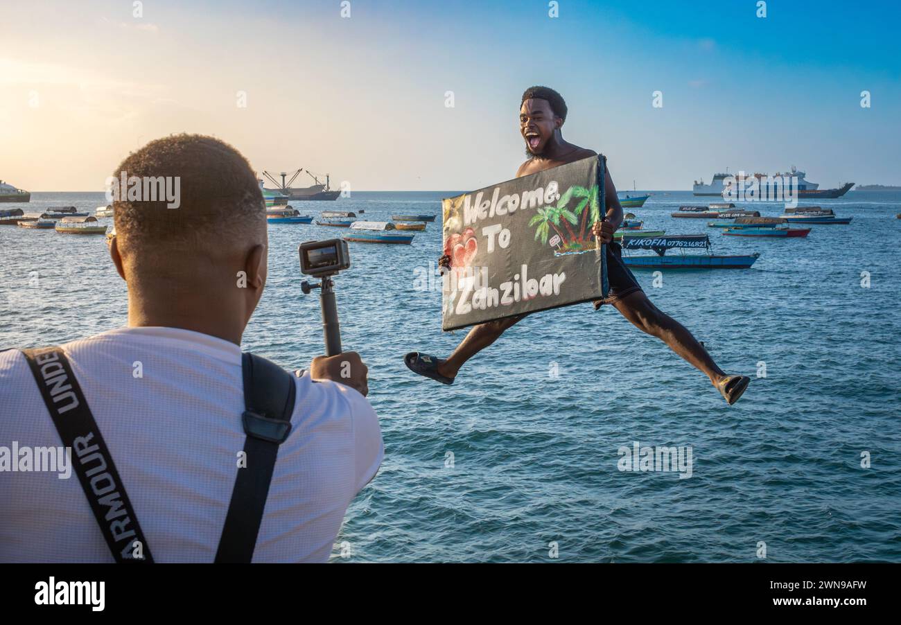 A tourist films a young man leaping into the sea with a sign reading ...