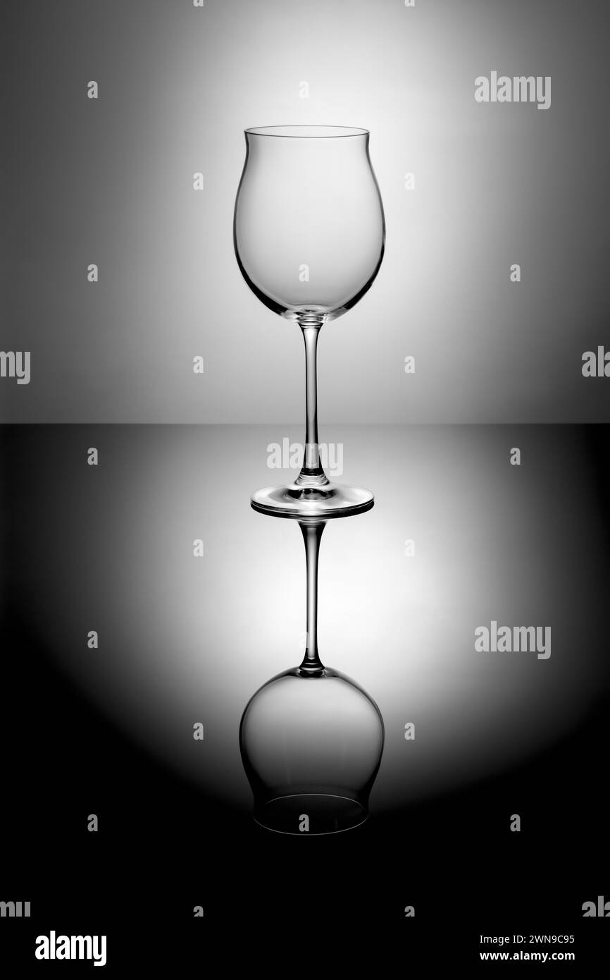 An empty wine glass with a symmetrical reflection on a shiny surface ...
