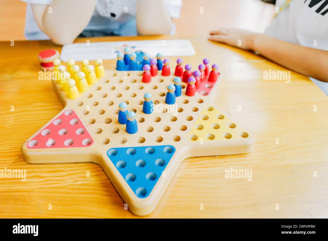 Kids are playing chinese checkers at a wooden table. Three-player ...