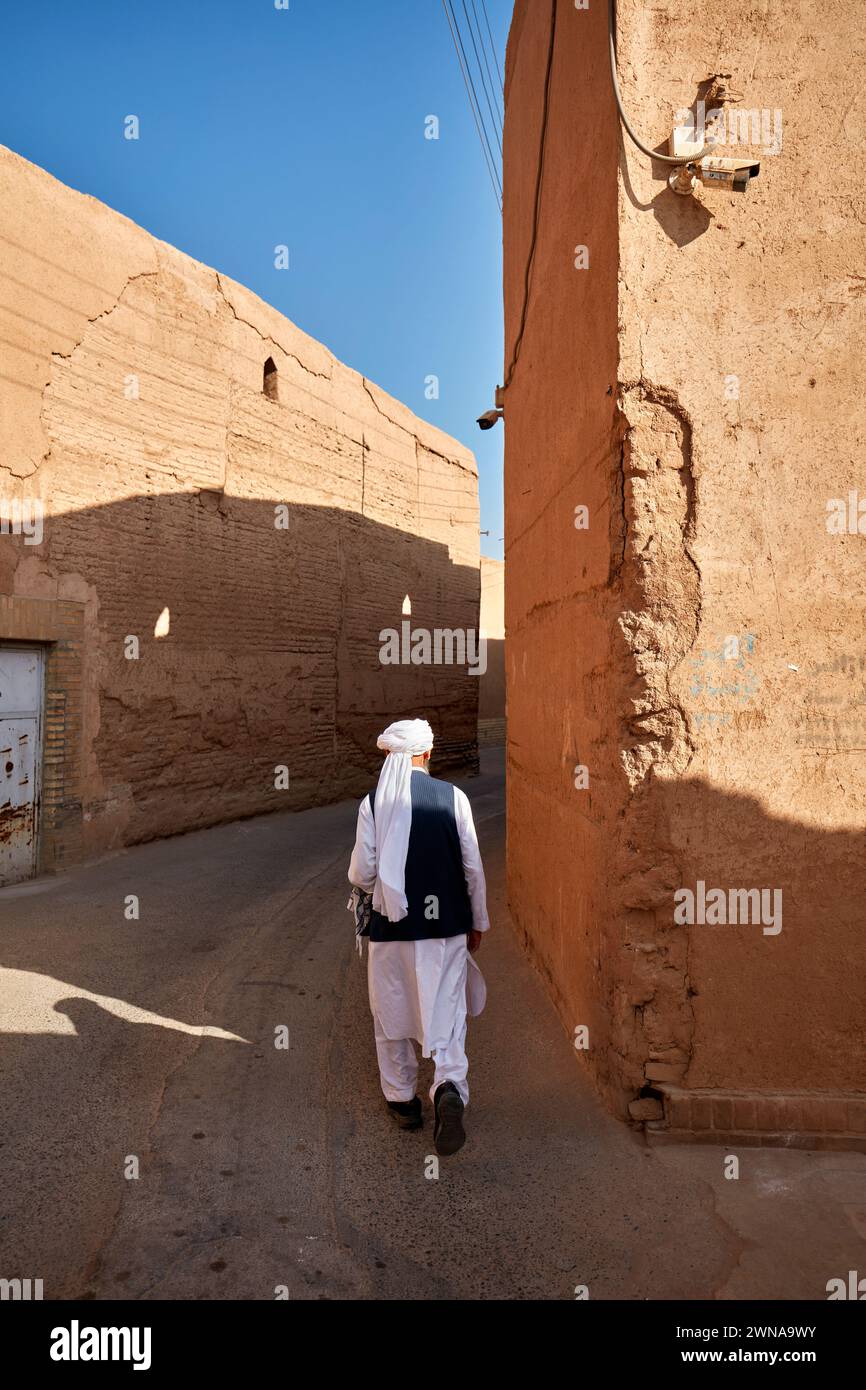 Iranian man in traditional attire walks in a narrow street in the old ...