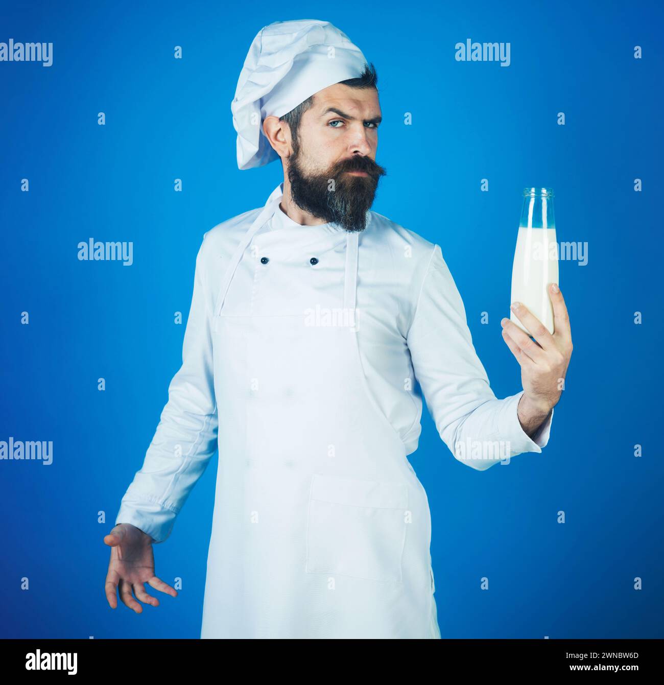 Bearded chef man in white uniform with bottle of milk drink. Male cook ...
