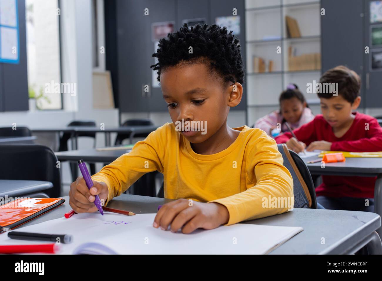 African American boy focused on drawing with a purple marker in a ...