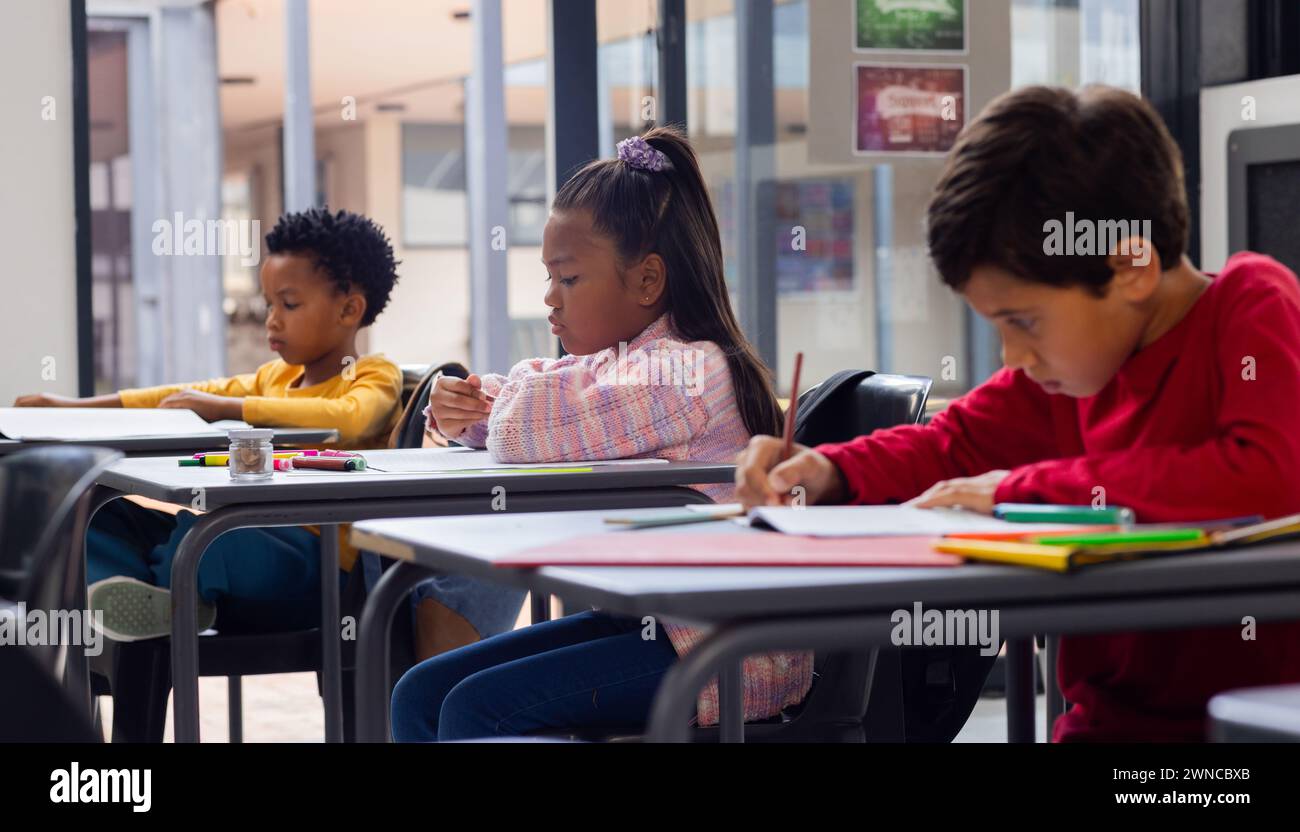Three children are focused on writing at desks in a school classroom ...