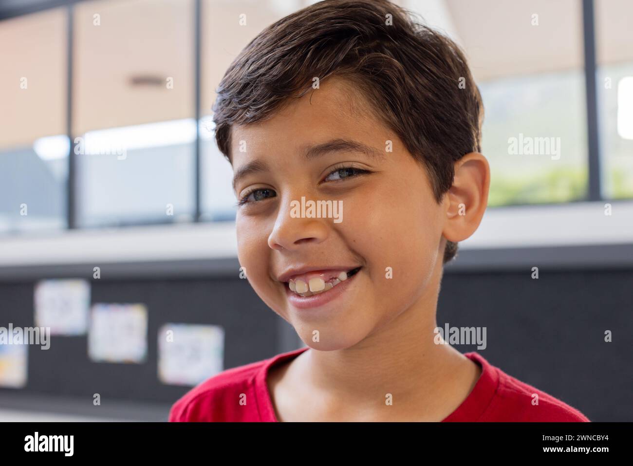 Biracial boy with a bright smile, wearing a red shirt in a school ...