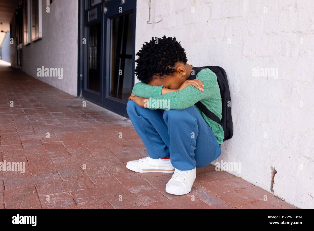 African American boy appears upset, sitting alone with his head down ...