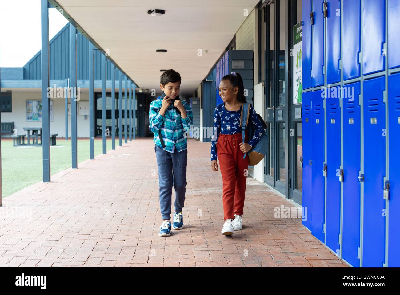 Biracial boy and girl walk through a school corridor, lockers lining ...