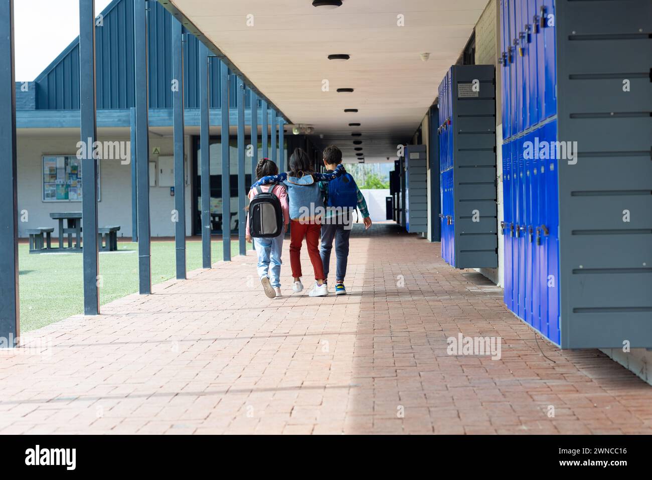Three children walk down a school corridor, arms around each other ...
