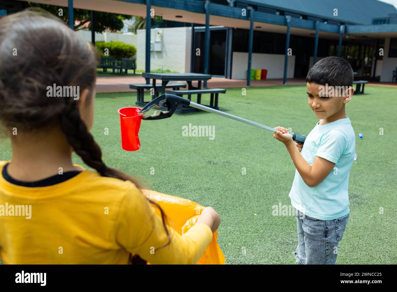 Biracial boy with a litter picker is cleaning up, facing a girl with a ...