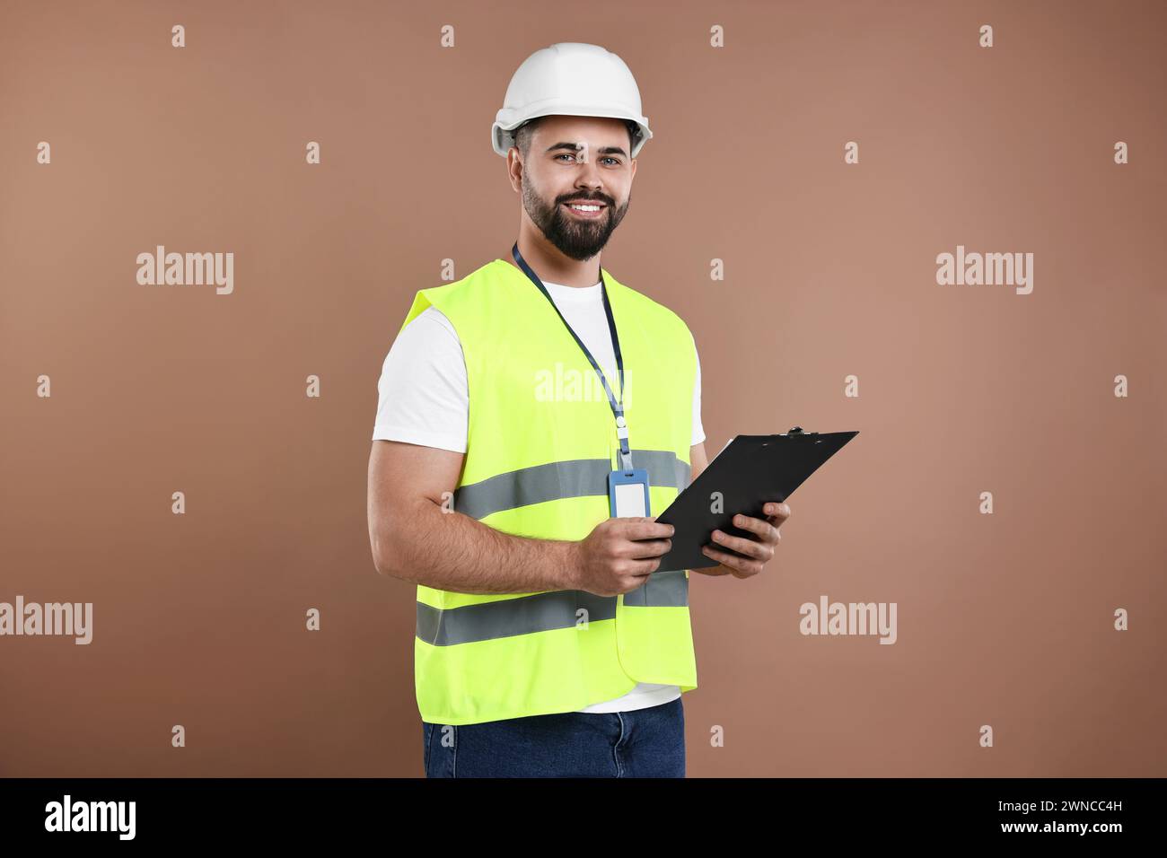 Engineer in hard hat holding clipboard on brown background Stock Photo ...