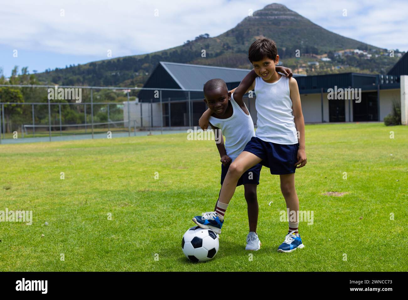 Biracial boy and African American boy play soccer outdoors in school ...