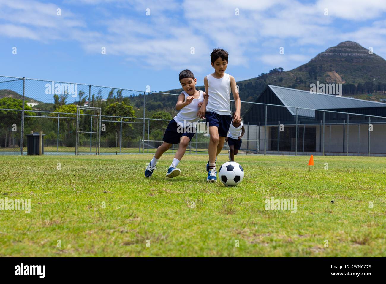 Two boys are playing soccer on a sunny day in school, with one chasing ...
