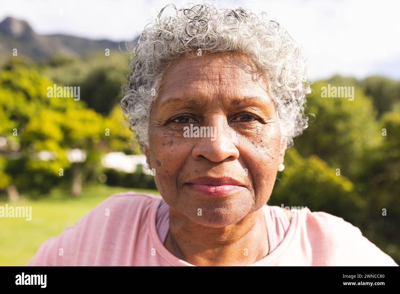 Senior biracial woman with curly gray hair and a gentle smile stands ...