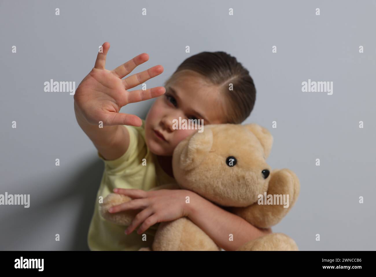 Child abuse. Girl with toy making stop gesture near grey wall ...