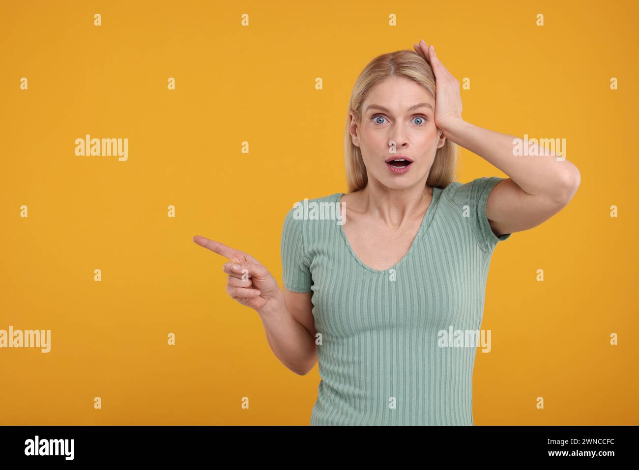 Surprised woman pointing at something on yellow background, space for ...