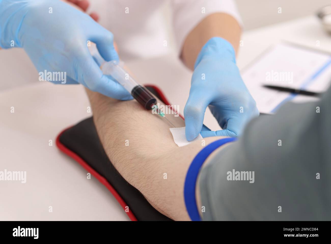 Doctor taking blood sample from patient with syringe at white table in ...