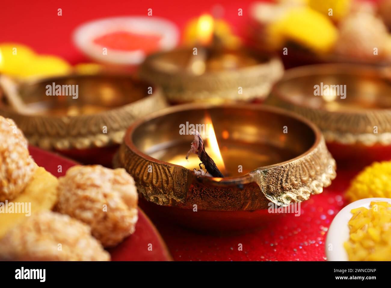 Diwali celebration. Diya lamps and tasty Indian sweets on shiny red ...