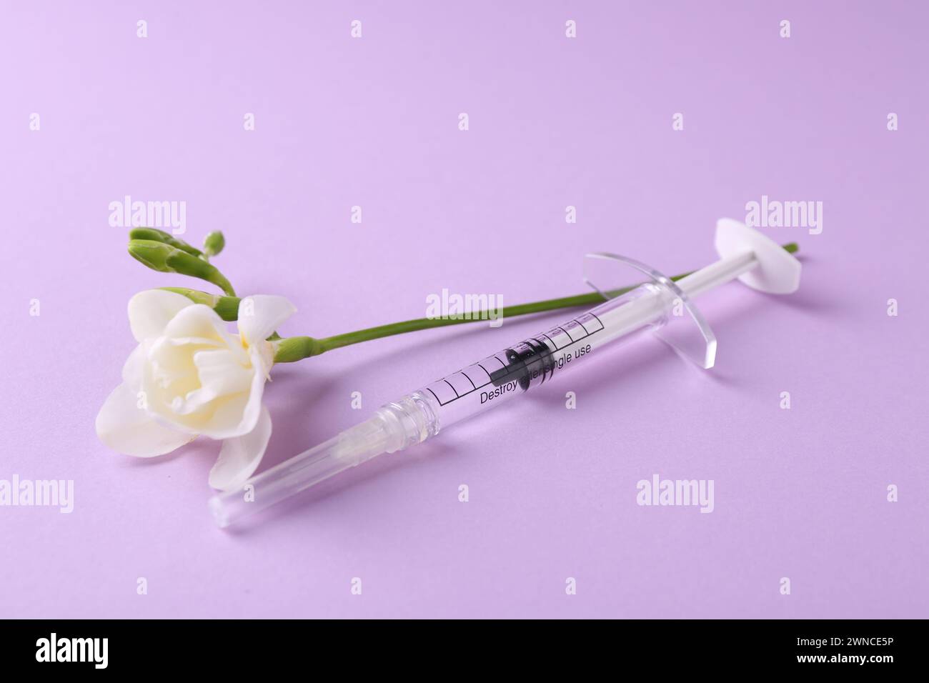 Cosmetology. Medical syringe and freesia flower on violet background ...