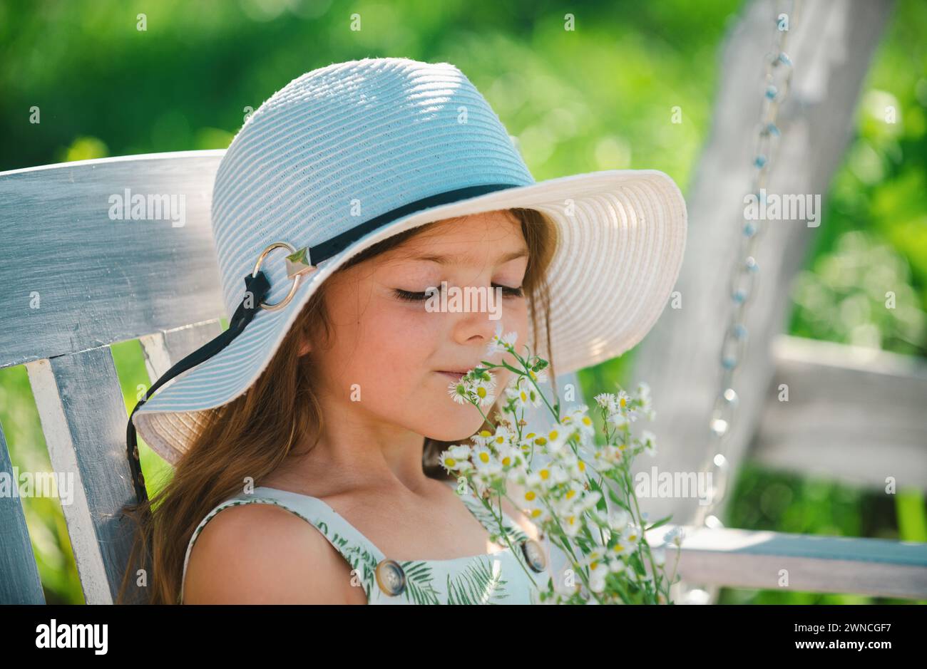 Little child girl is smelling flowers on green backyard. Adorable kid ...