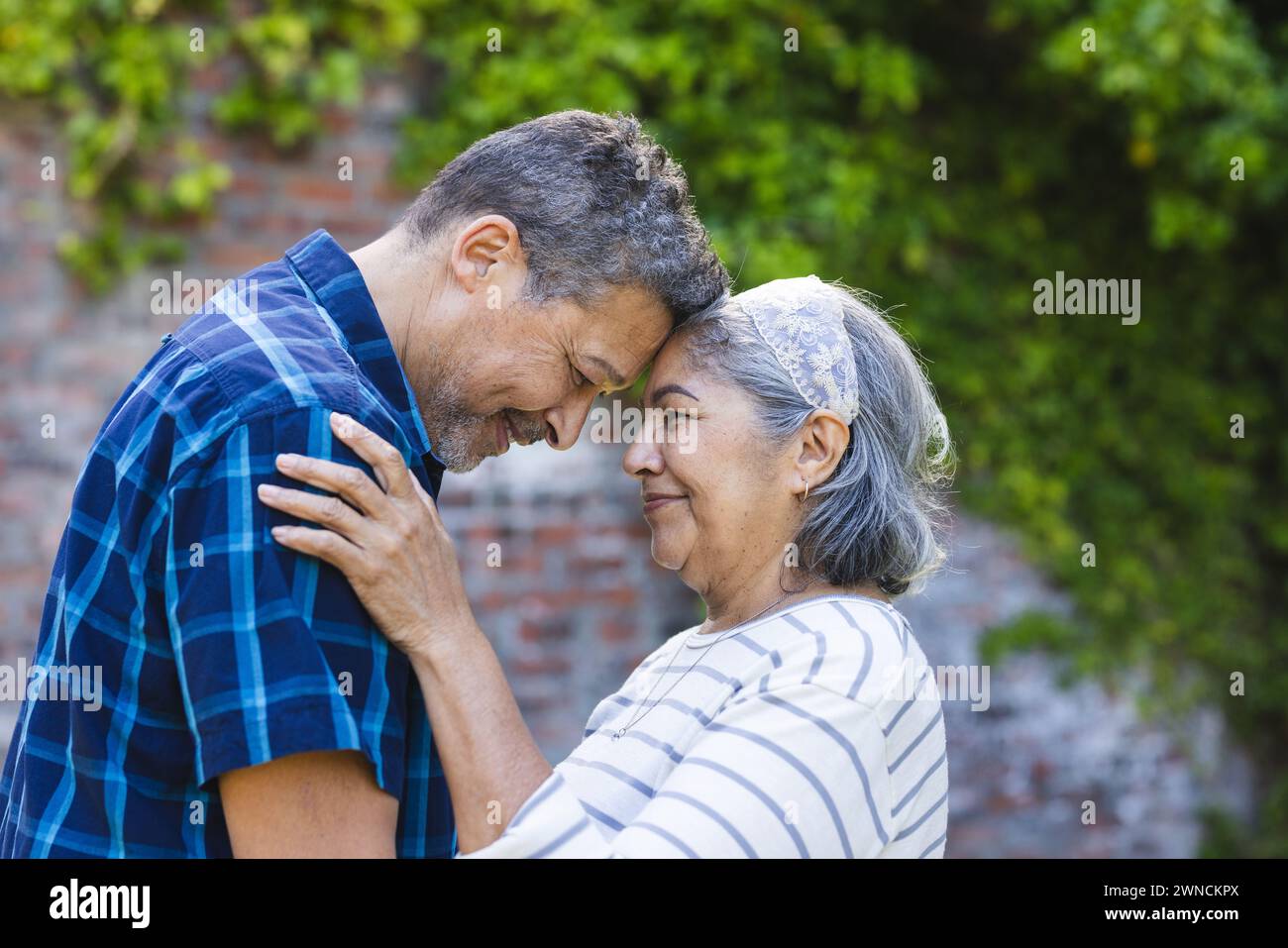 Senior biracial couple shares a tender moment, foreheads touching with ...