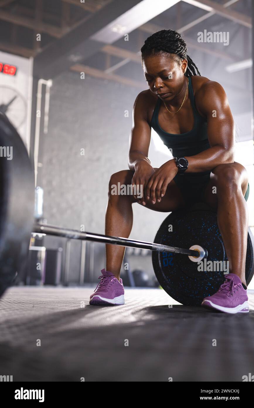 A strong, fit biracial woman prepares to lift a barbell at the gym with ...