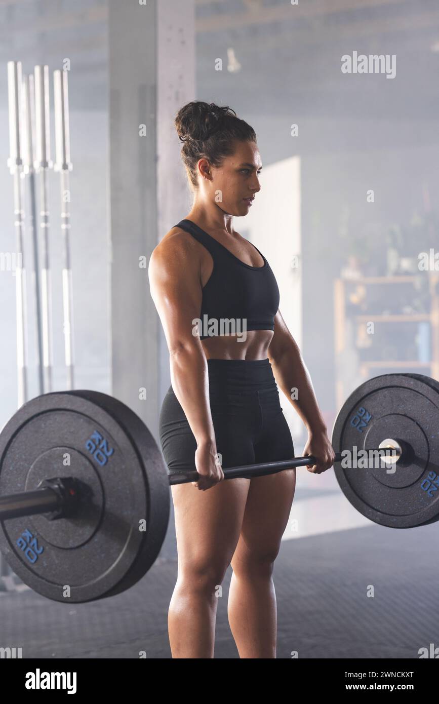 Young **strong** fit biracial woman lifts weights at a gym, showcasing ...