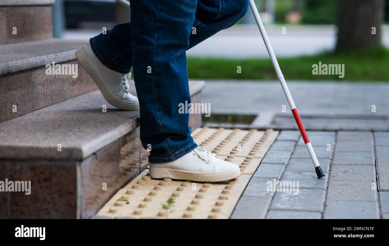 Close-up of female foot, walking stick and tactile tiles. Blind woman ...