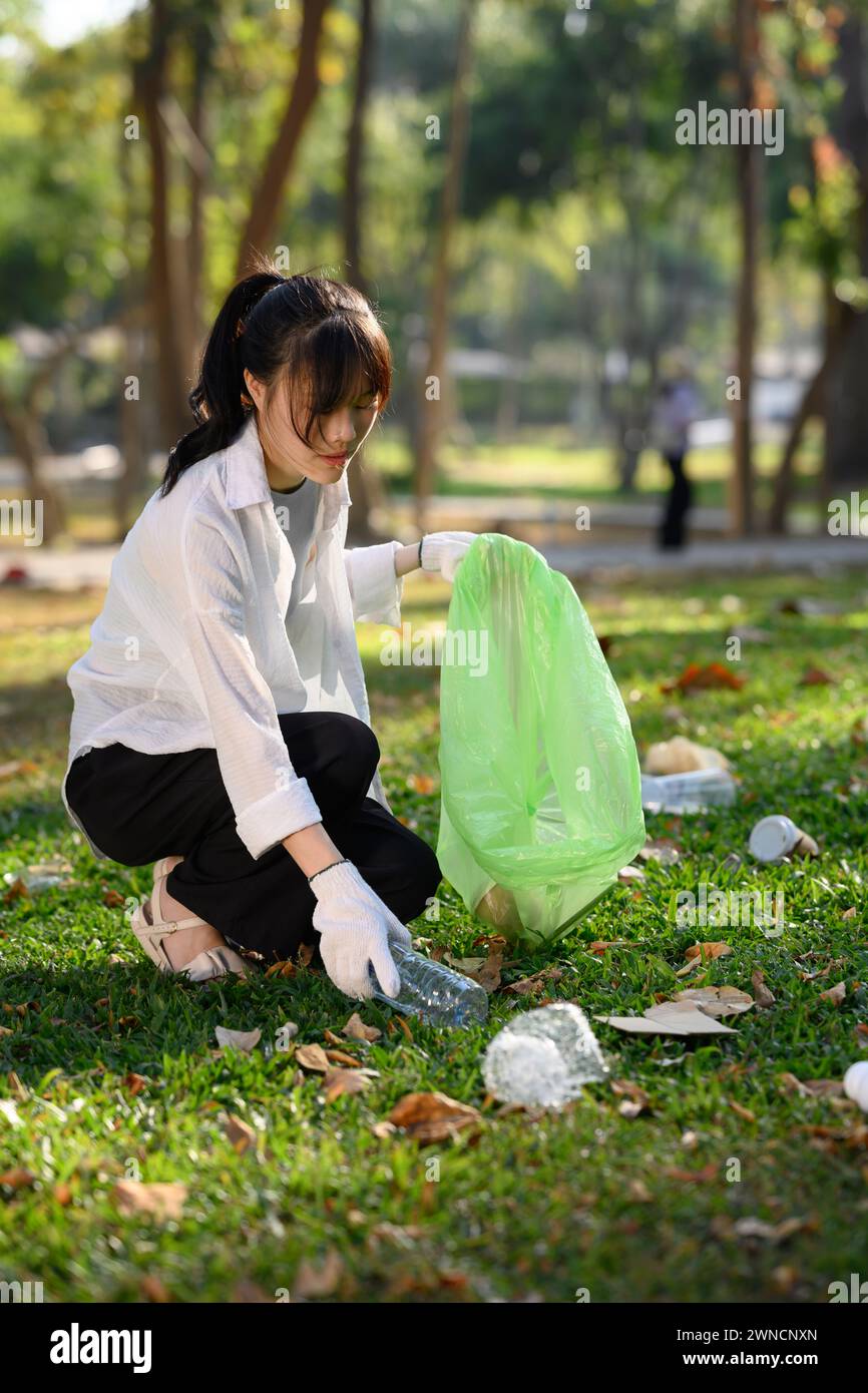 Shot of young lady collecting plastic bottles, cleaning up nature ...