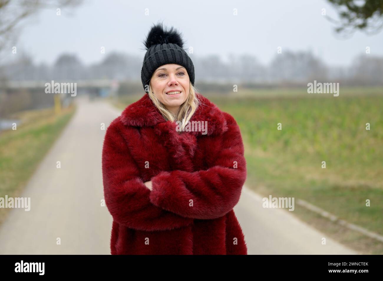 Attractive blonde lady wearing a red jacket and black bobble hat stands ...