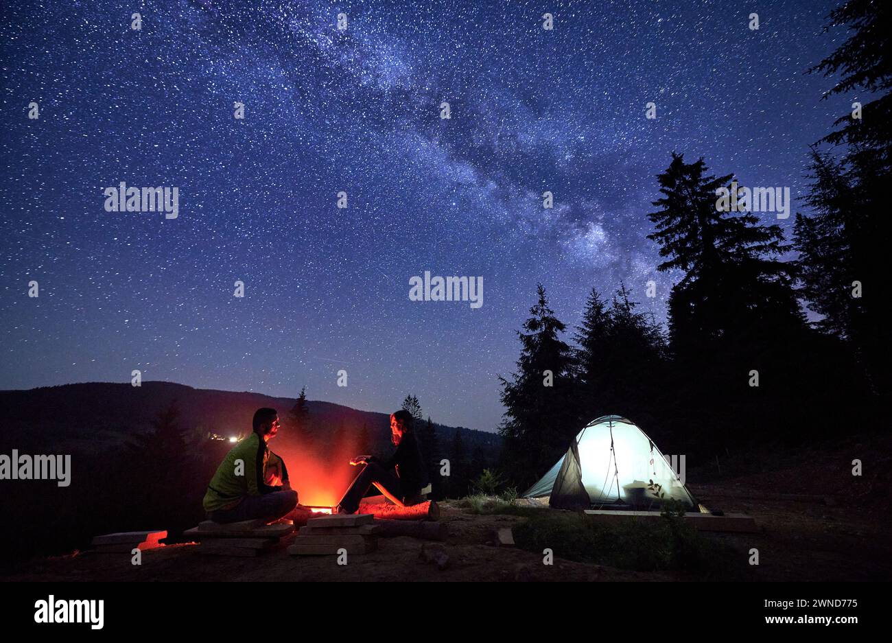 Night-time sojourn in mountains, beneath starry sky. Man and woman ...