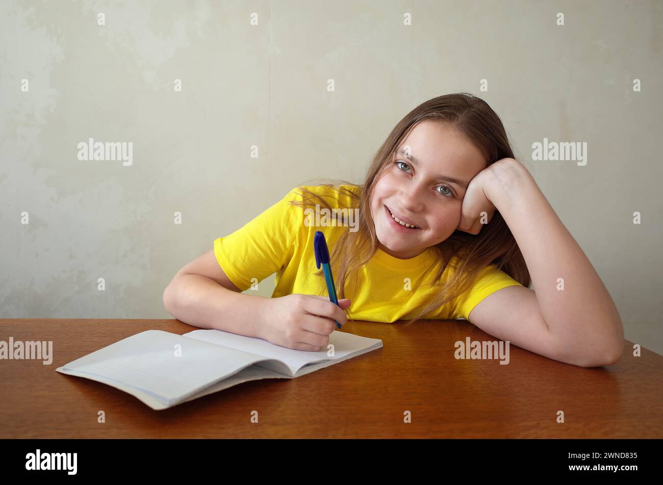 Happy girl writing in notebook placed on wooden desktop with background ...