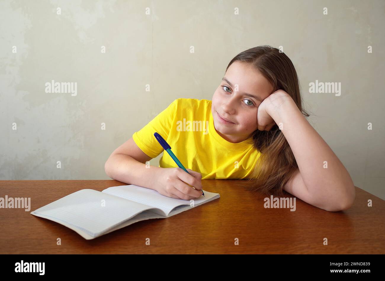 Happy girl writing in notebook placed on wooden desktop with background ...