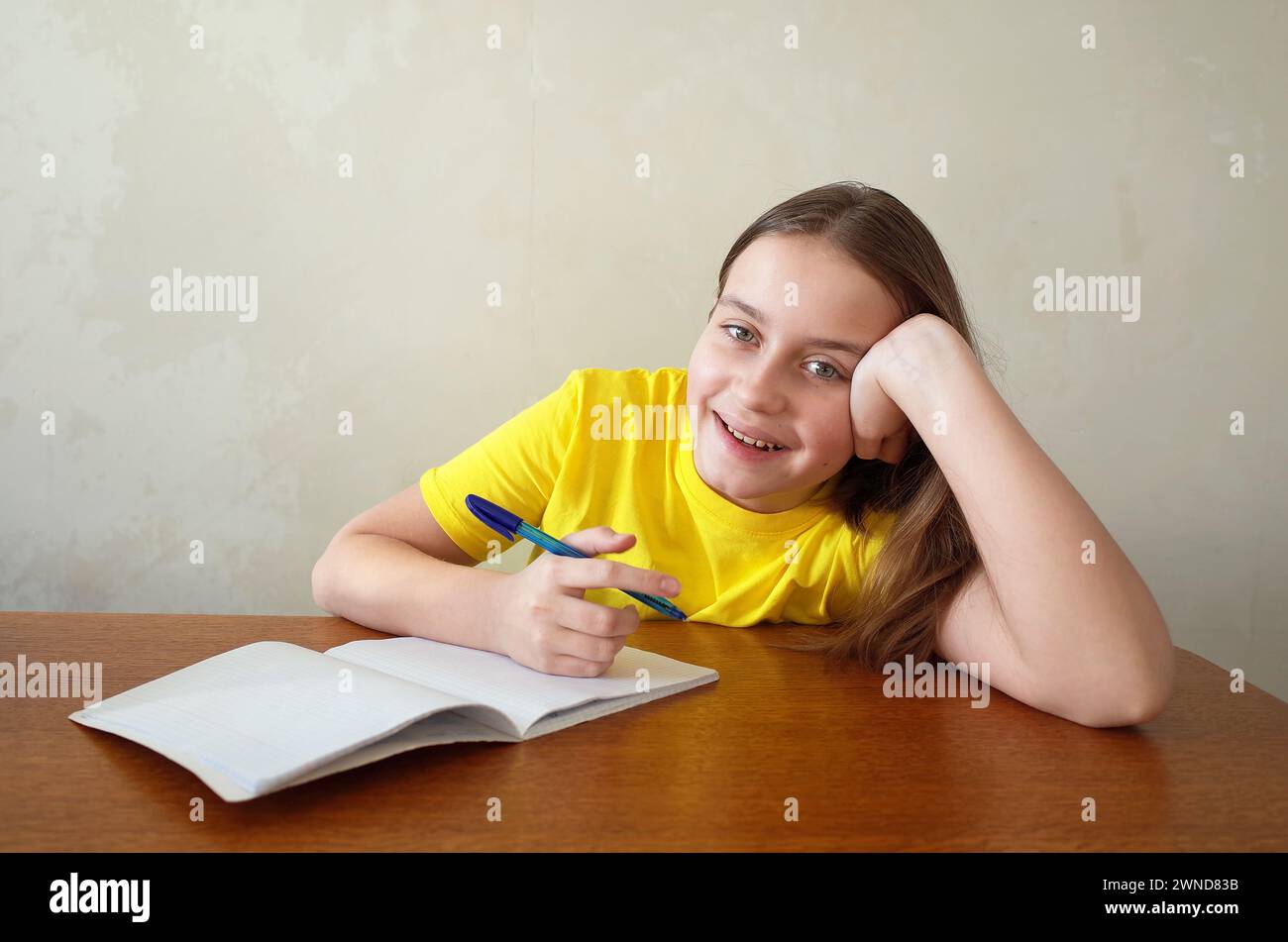Happy girl writing in notebook placed on wooden desktop with background ...