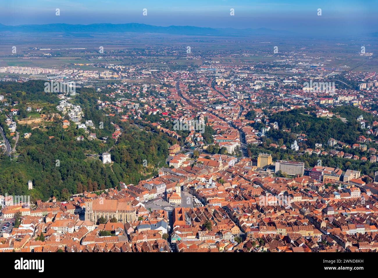 Cityscape with numerous brown rooftops and lush trees in the distance ...