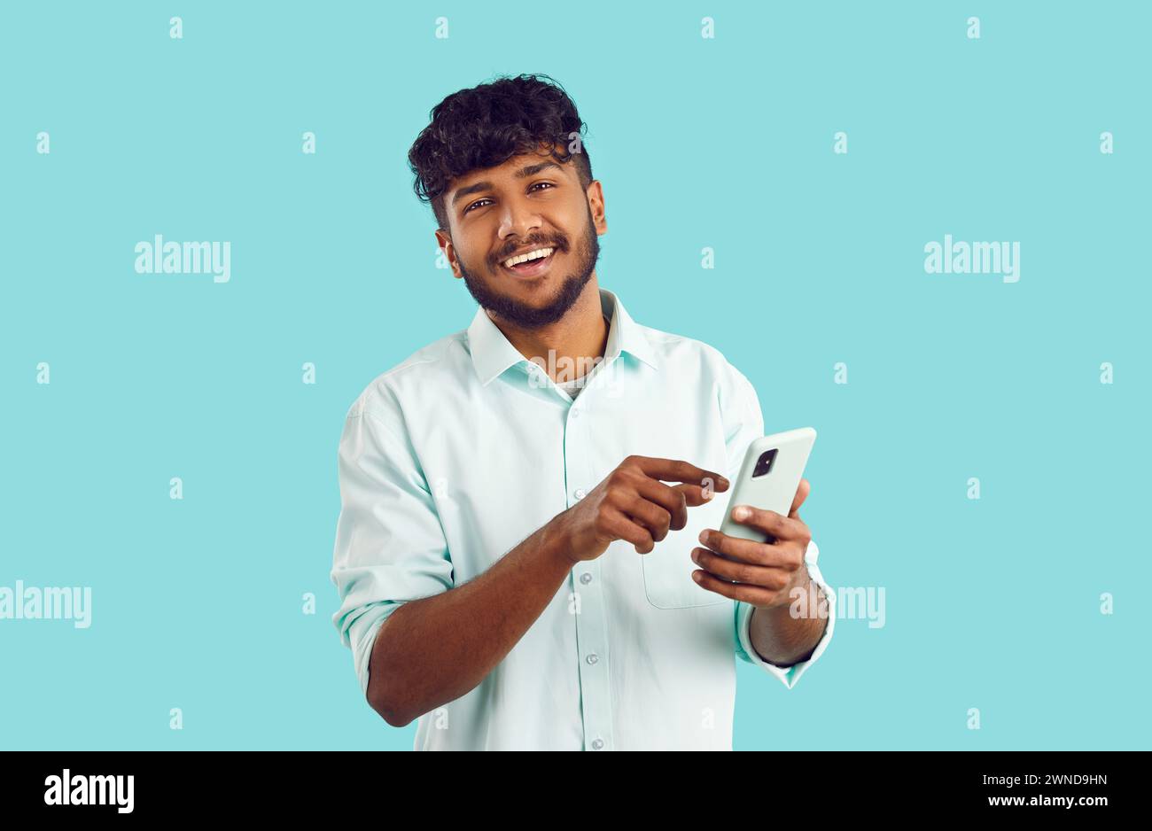 Young Indian man holding mobile phone and smiling looking at camera ...