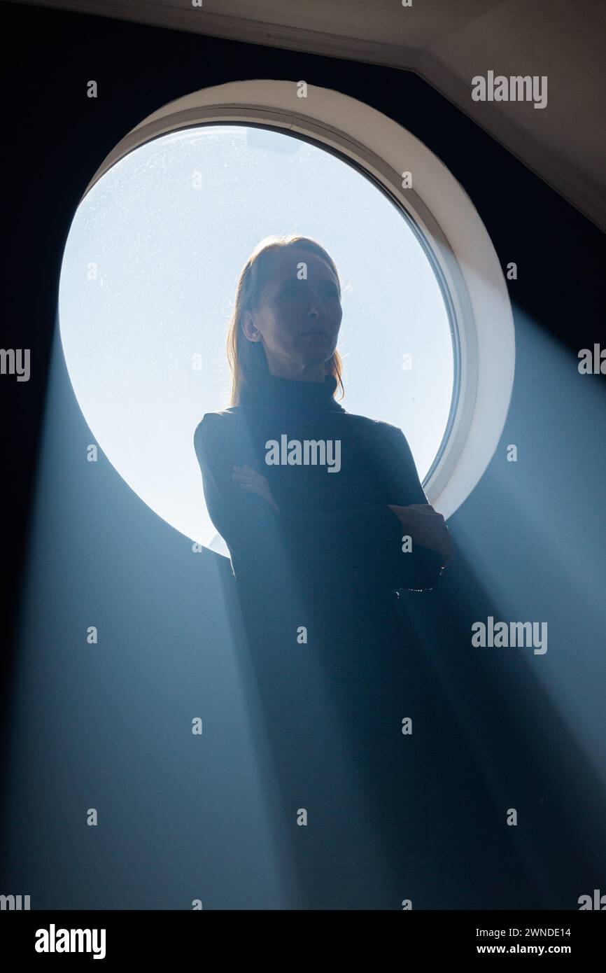 Adult woman standing with her back to the window in the rays of the sun ...