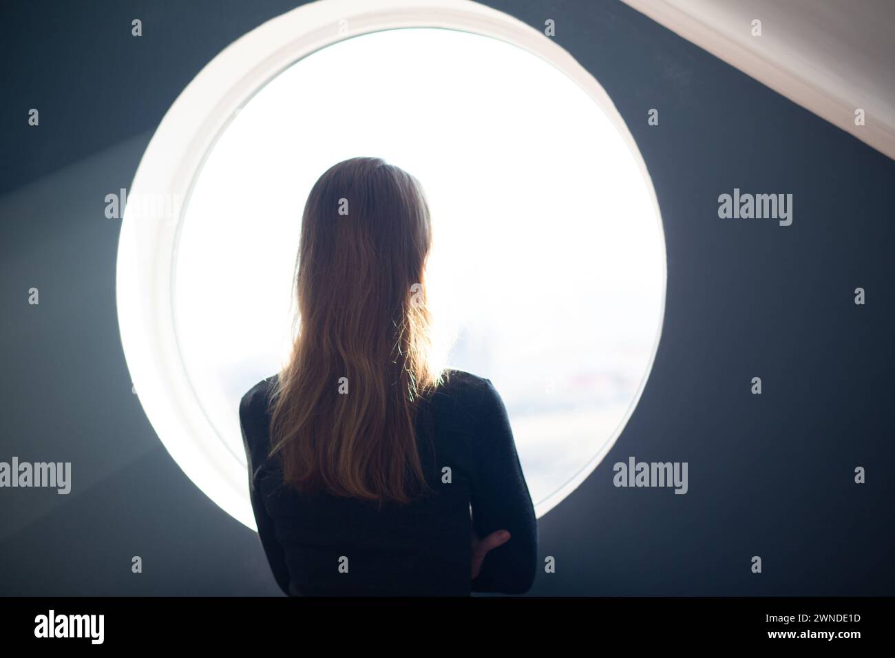 A woman stands facing the window, bathed in the rays of the sun. The ...